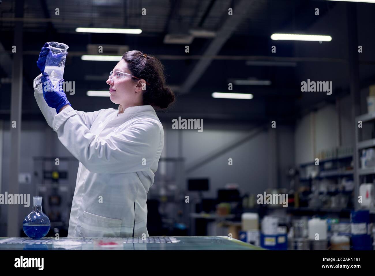 Young brunette lab woman in white coat with flask with blue liquid in ...