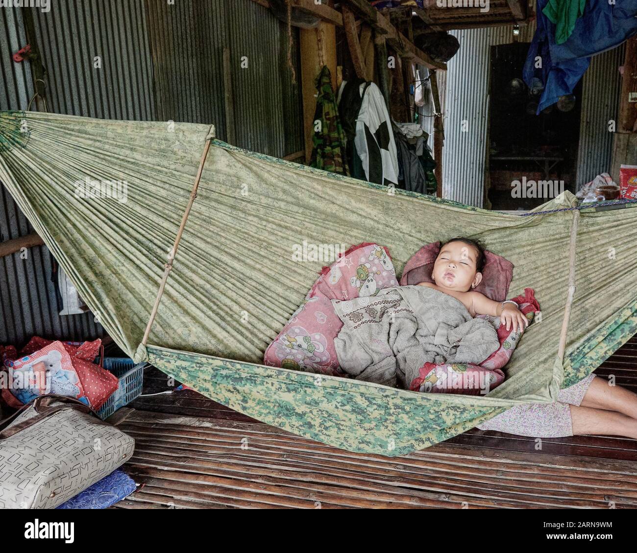 Cambodian baby being gently rocked to sleep in shade under the family’s ...