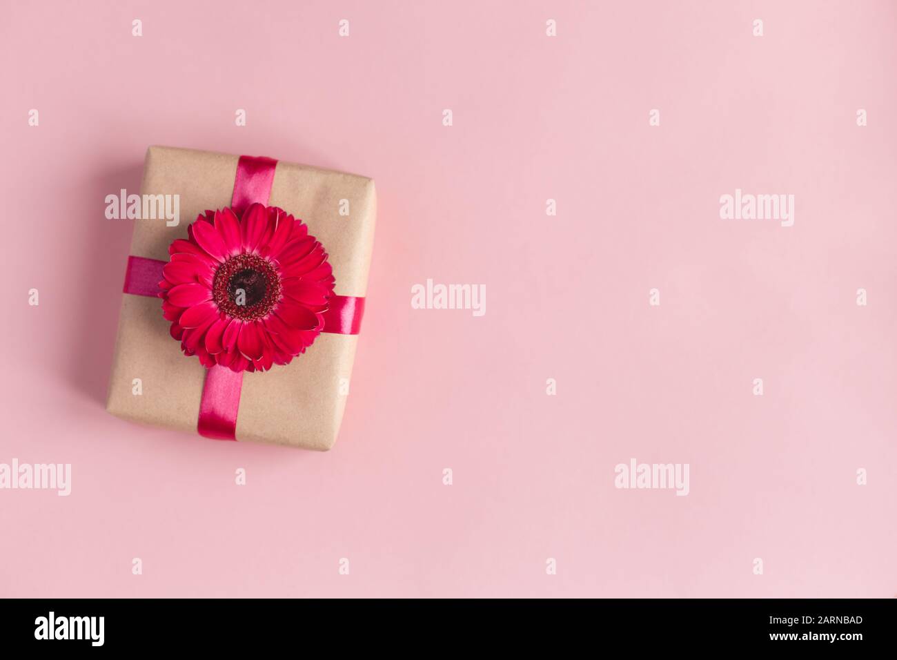 Craft gift box with pink flower and ribbon on a pastel pink background ...