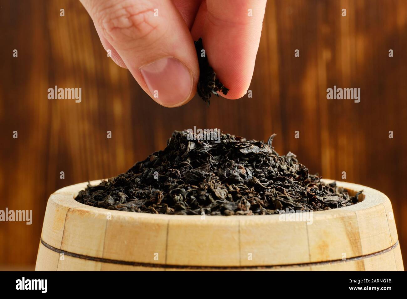 The hand pours tea into a keg against a burnt wooden background. Close ...