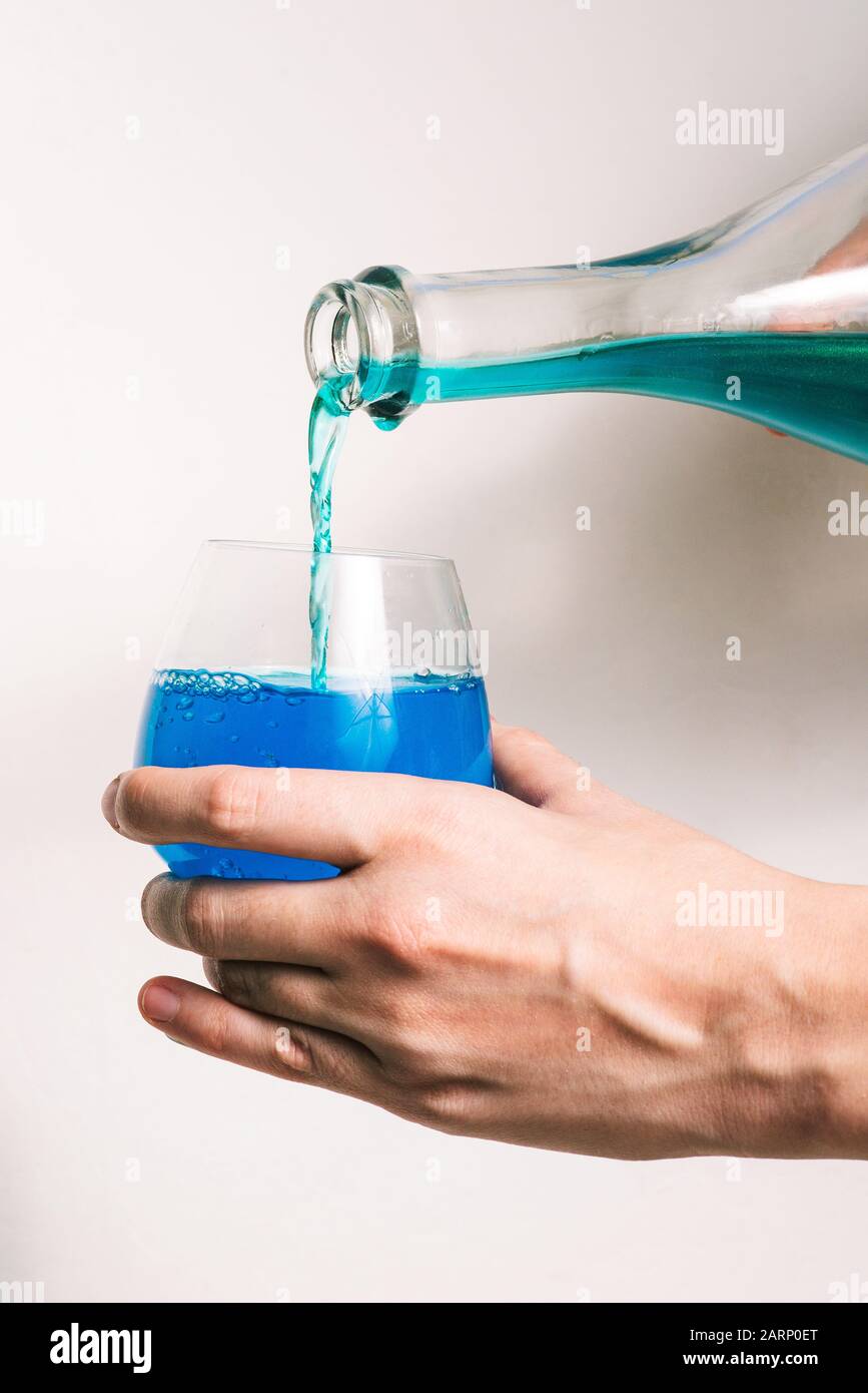 Blue liquid from a glass bottle flows into a wine glass. Alcoholic ...