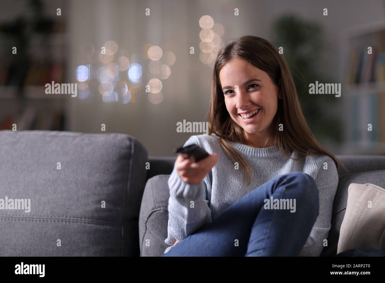 Happy woman in the night watching tv sitting on a couch in the living ...