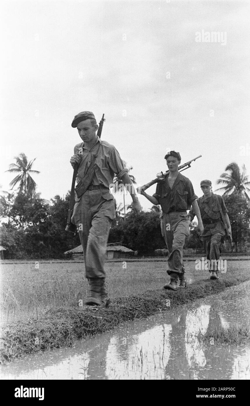 Three Dutch soldiers walk across a dike in a rice field. The middle one ...
