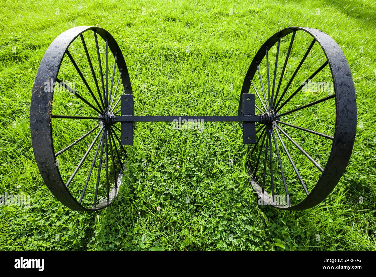 Vintage black metal wheels on one axis stand on grass at sunny day ...