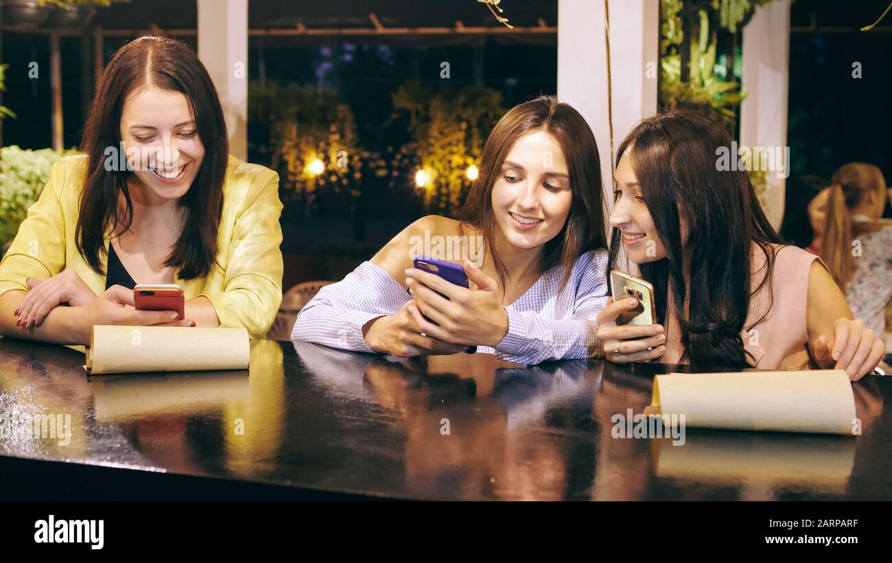 Three pretty girls are laughing during look over photos on phones at ...