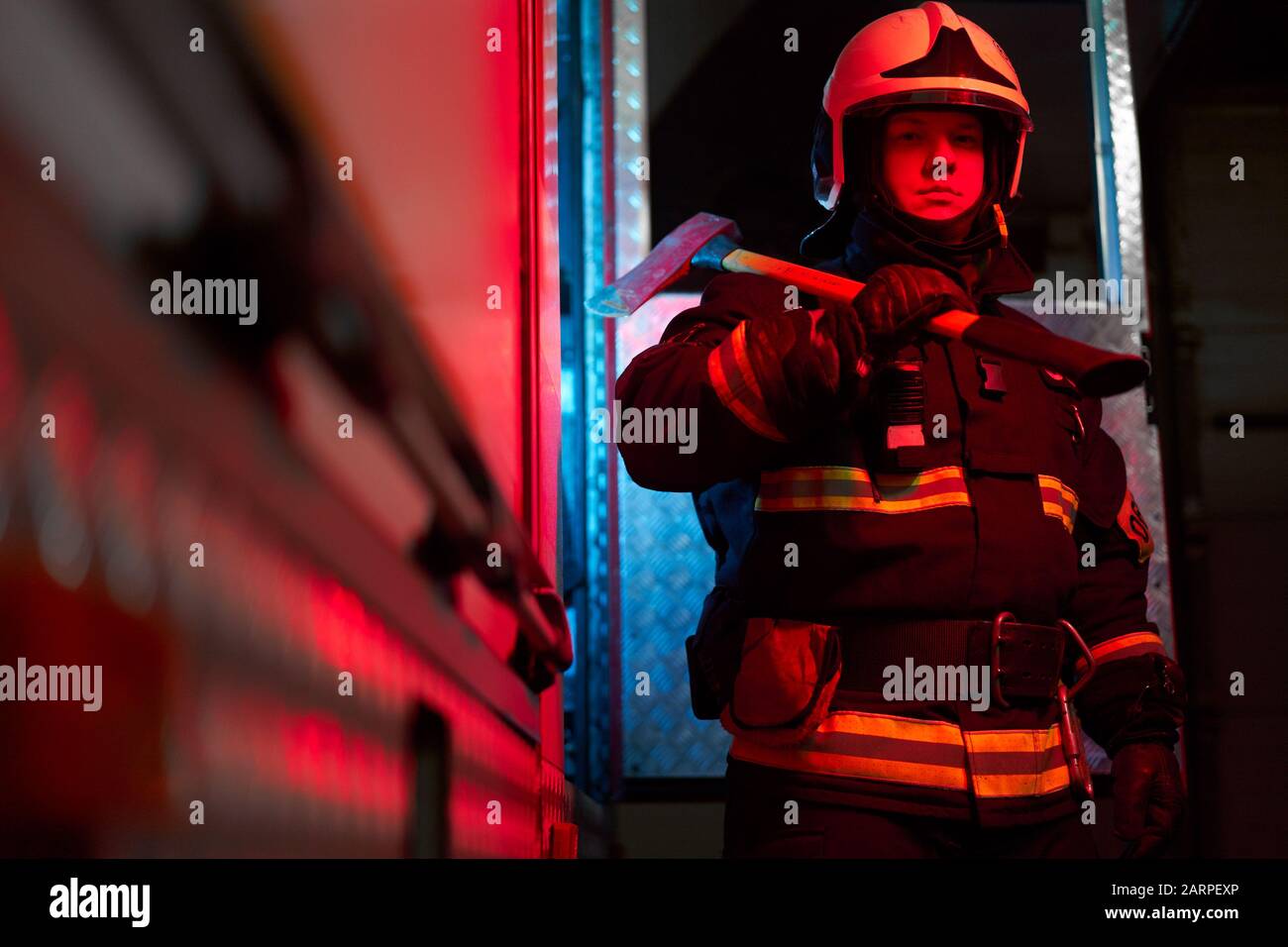 Firefighter man with hammer on his shoulder standing near fire engine ...