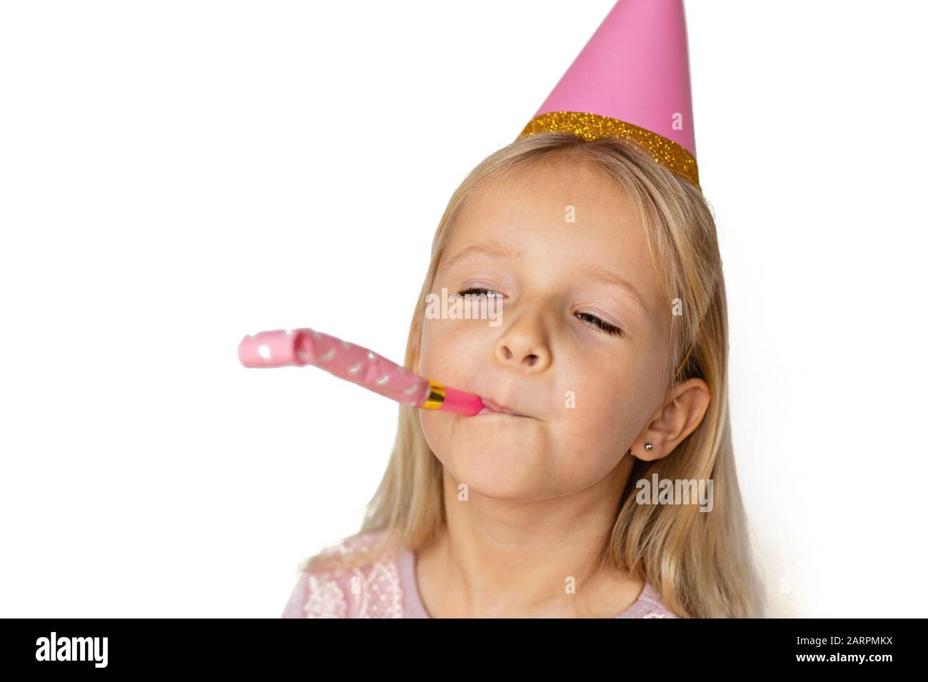 Small child in pink hat blowing in birthday pipe on white background ...