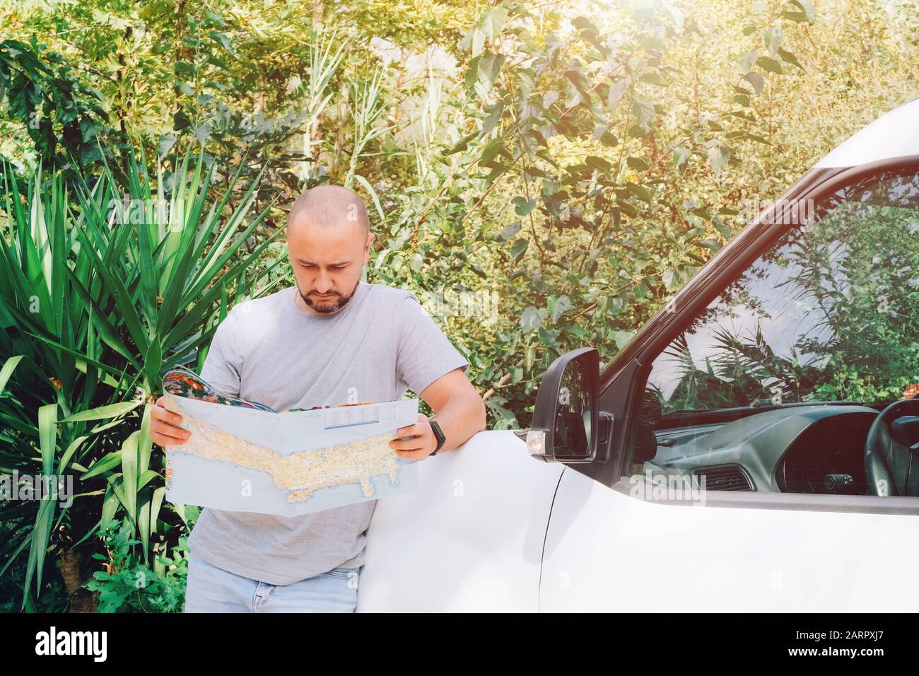 A young man stands near the car with a map of the area in his hands ...