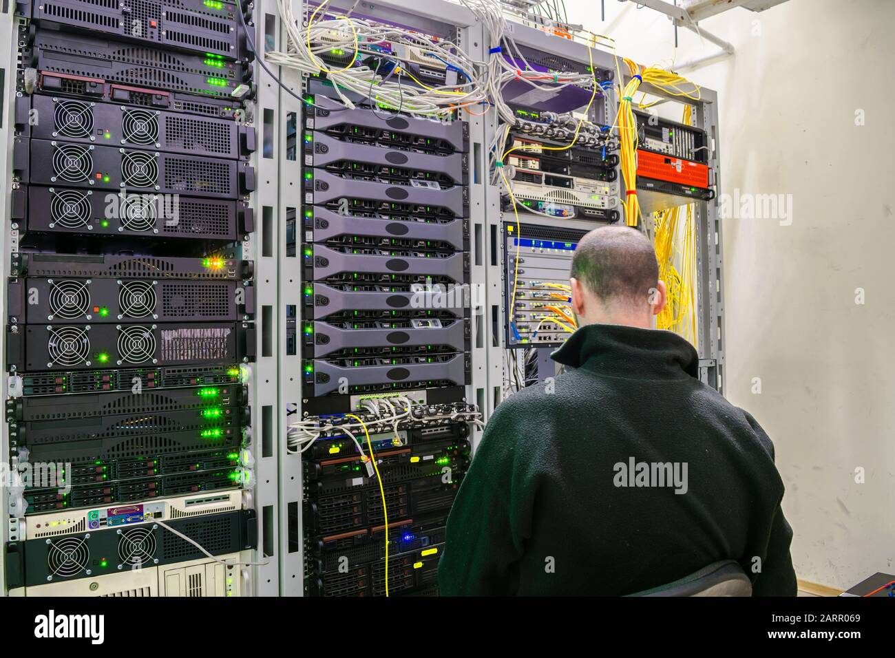 A man is sitting on a chair in the server room of the data center. The ...