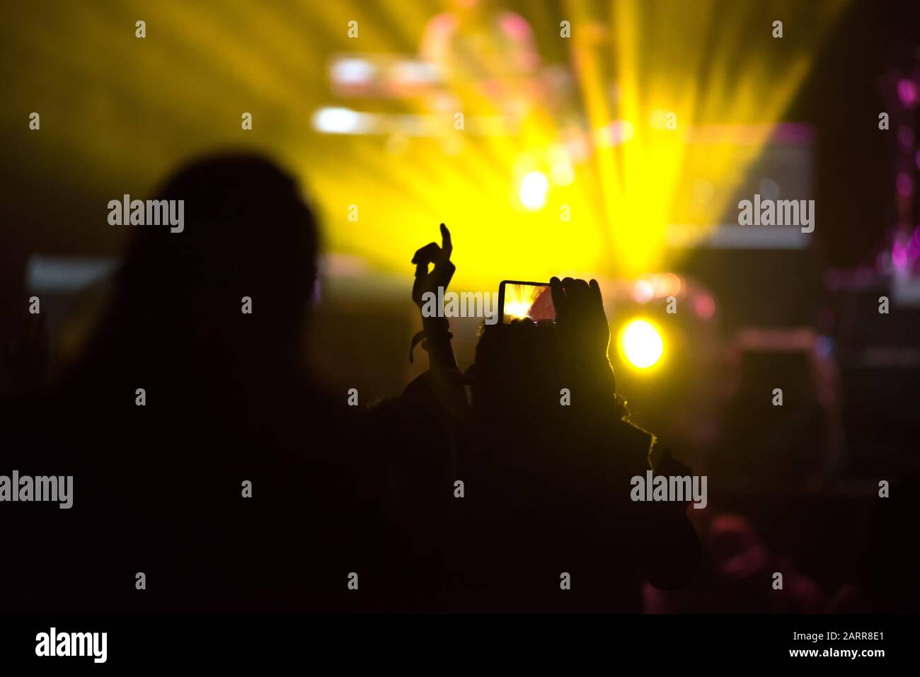 Silhouette of raised hands holding a smart phone recording music ...