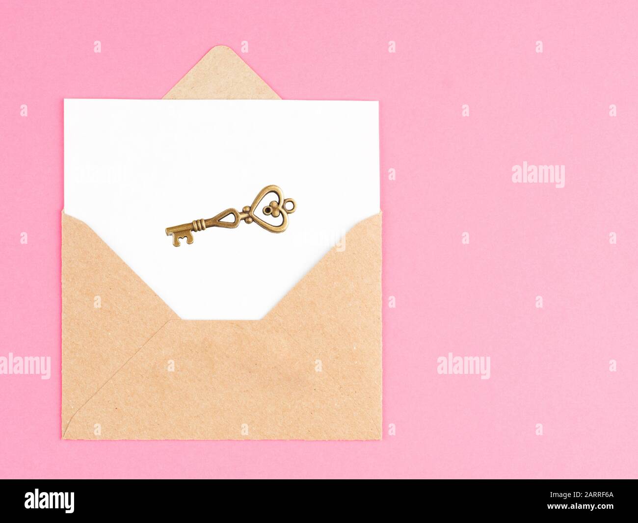 Kraft envelope with a white sheet and antique key on a pink background ...