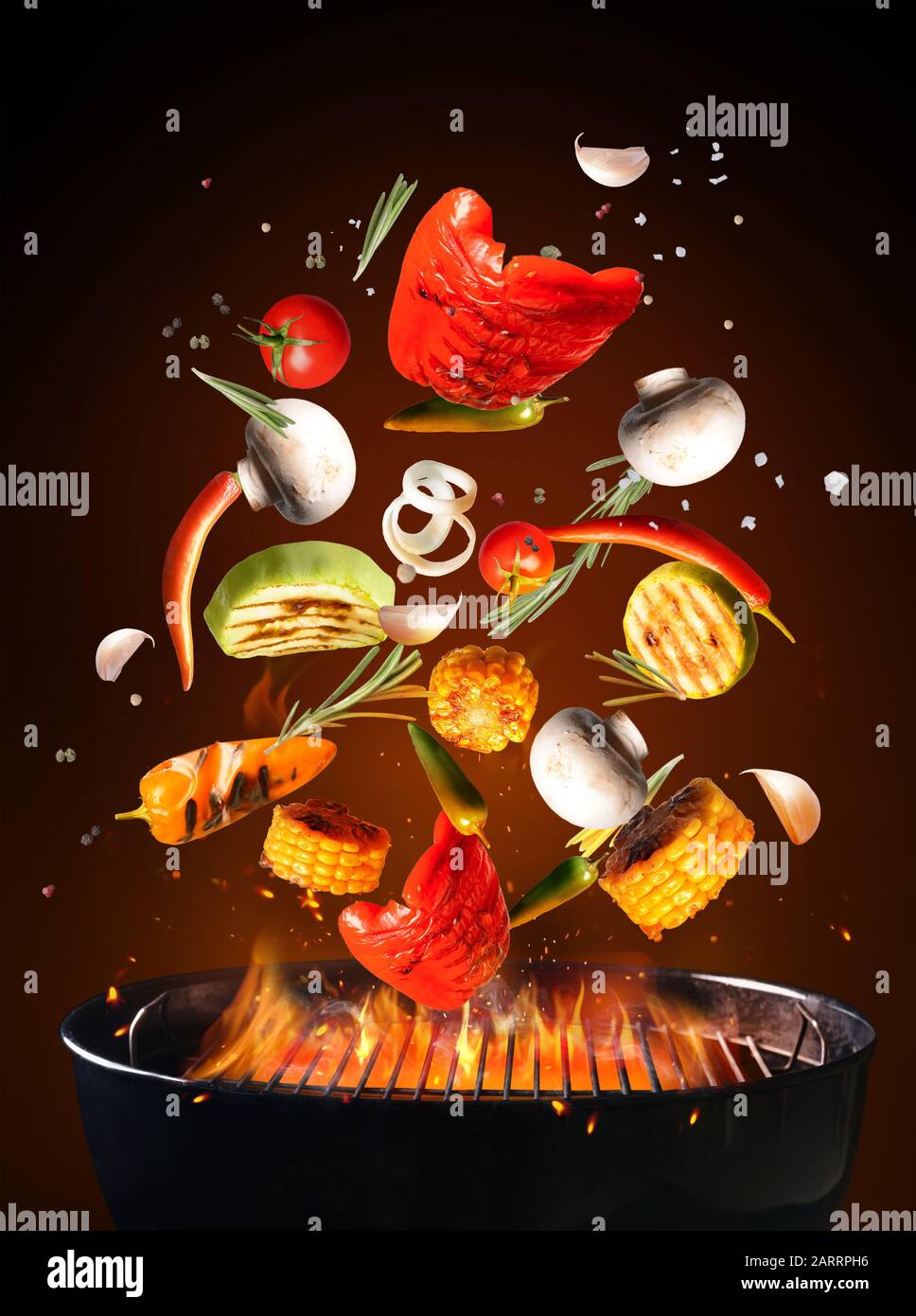 Falling tasty vegetables and spices on barbecue grill with flame ...