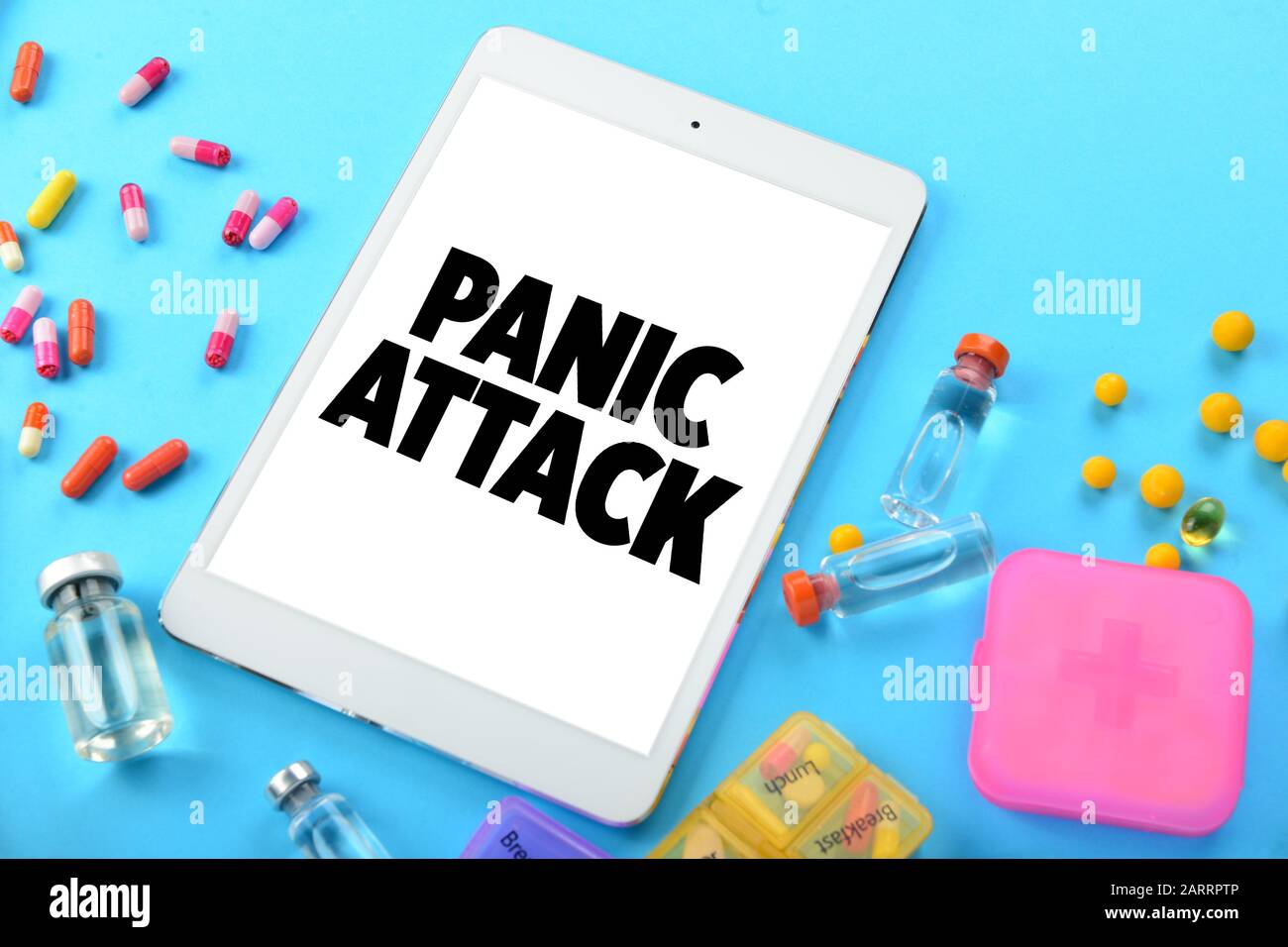 Tablet computer with text PANIC ATTACK on screen and medicines on color ...