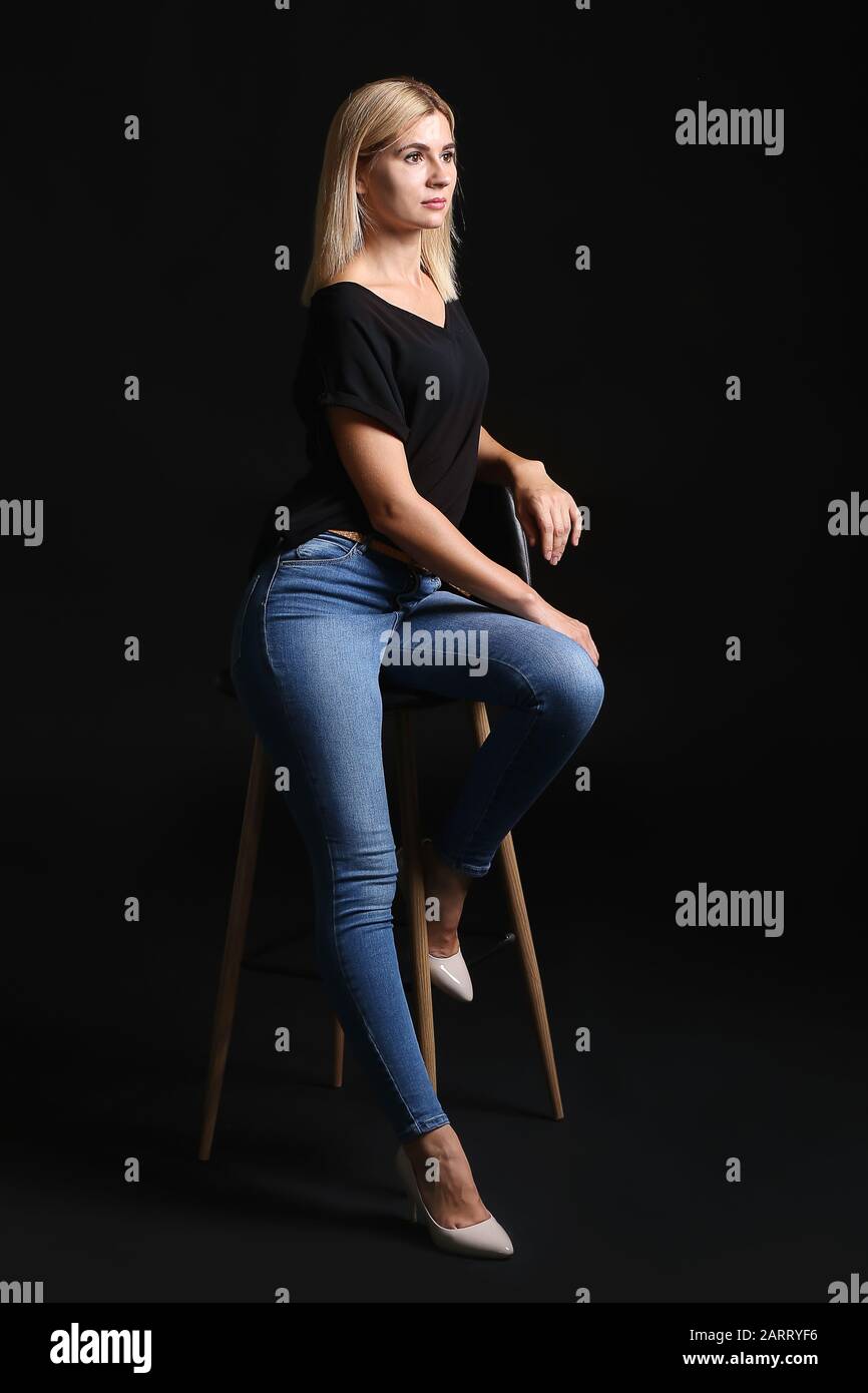 Beautiful stylish woman sitting on chair against dark background Stock ...