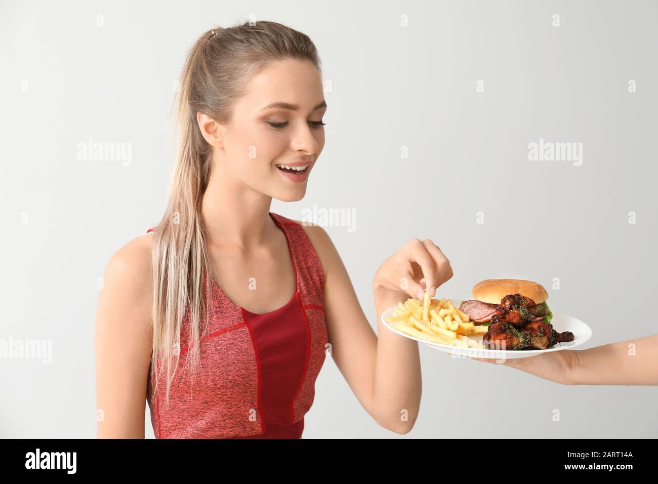 Sporty woman eating unhealthy food on light background. Diet concept ...