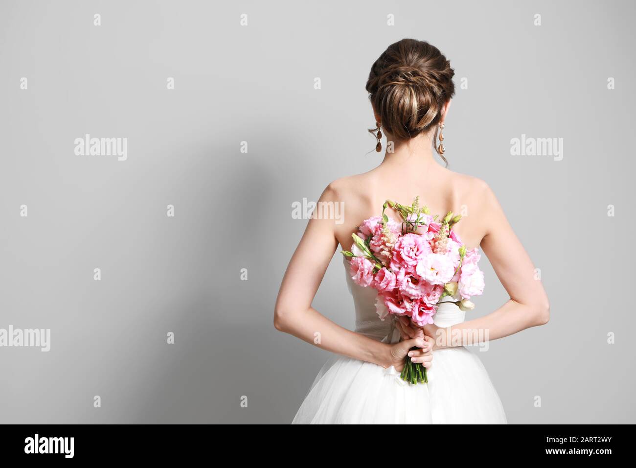 Beautiful young bride with wedding bouquet on grey background, back ...