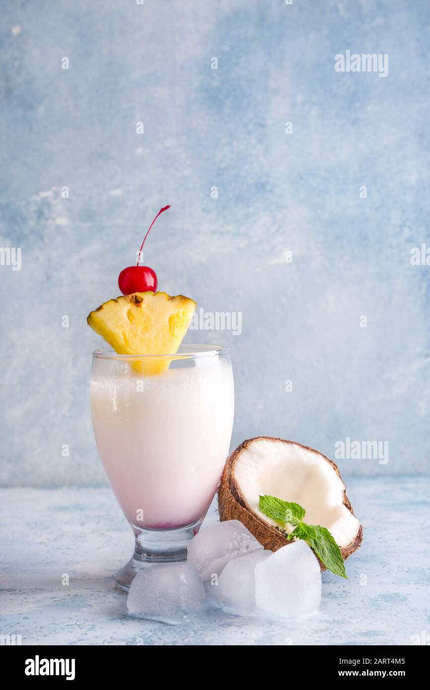 Glass of tasty Pina Colada cocktail, ice cubes and coconut on table ...