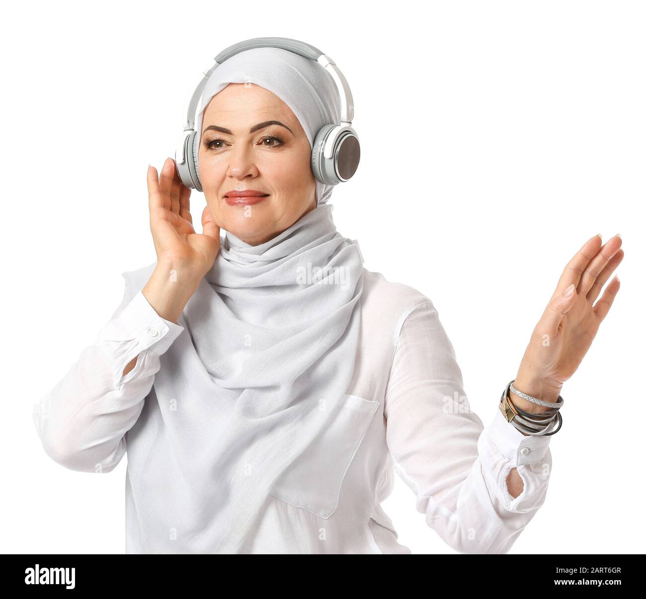 Beautiful mature Muslim woman listening to music on white background ...