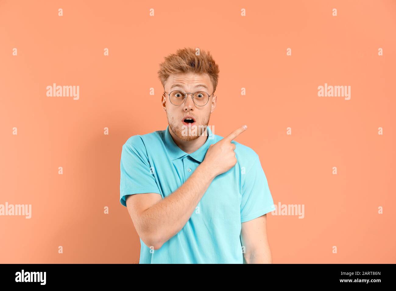 Portrait of surprised man pointing at something on color background ...