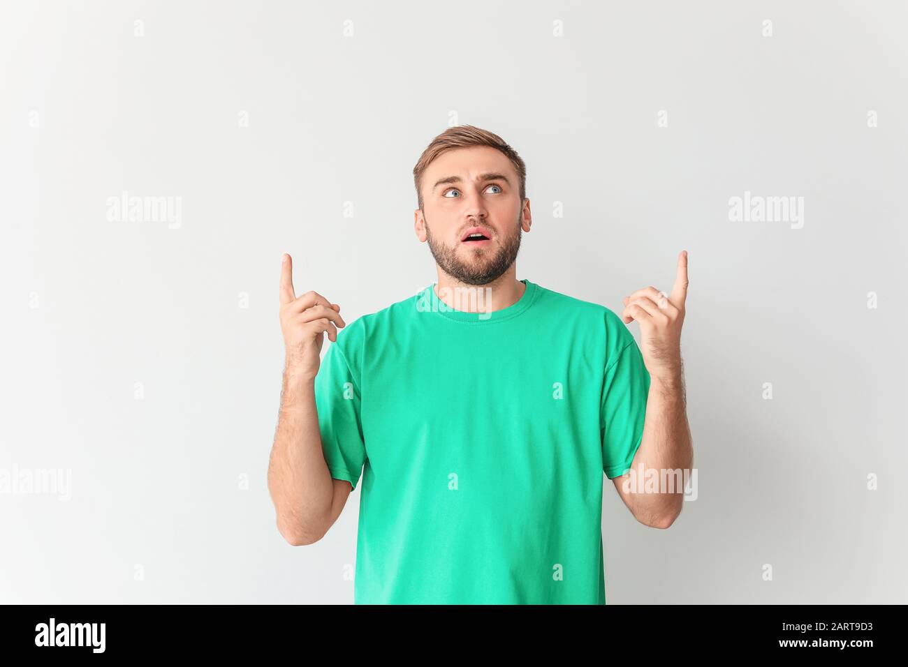 Surprised young man pointing at something on light background Stock ...
