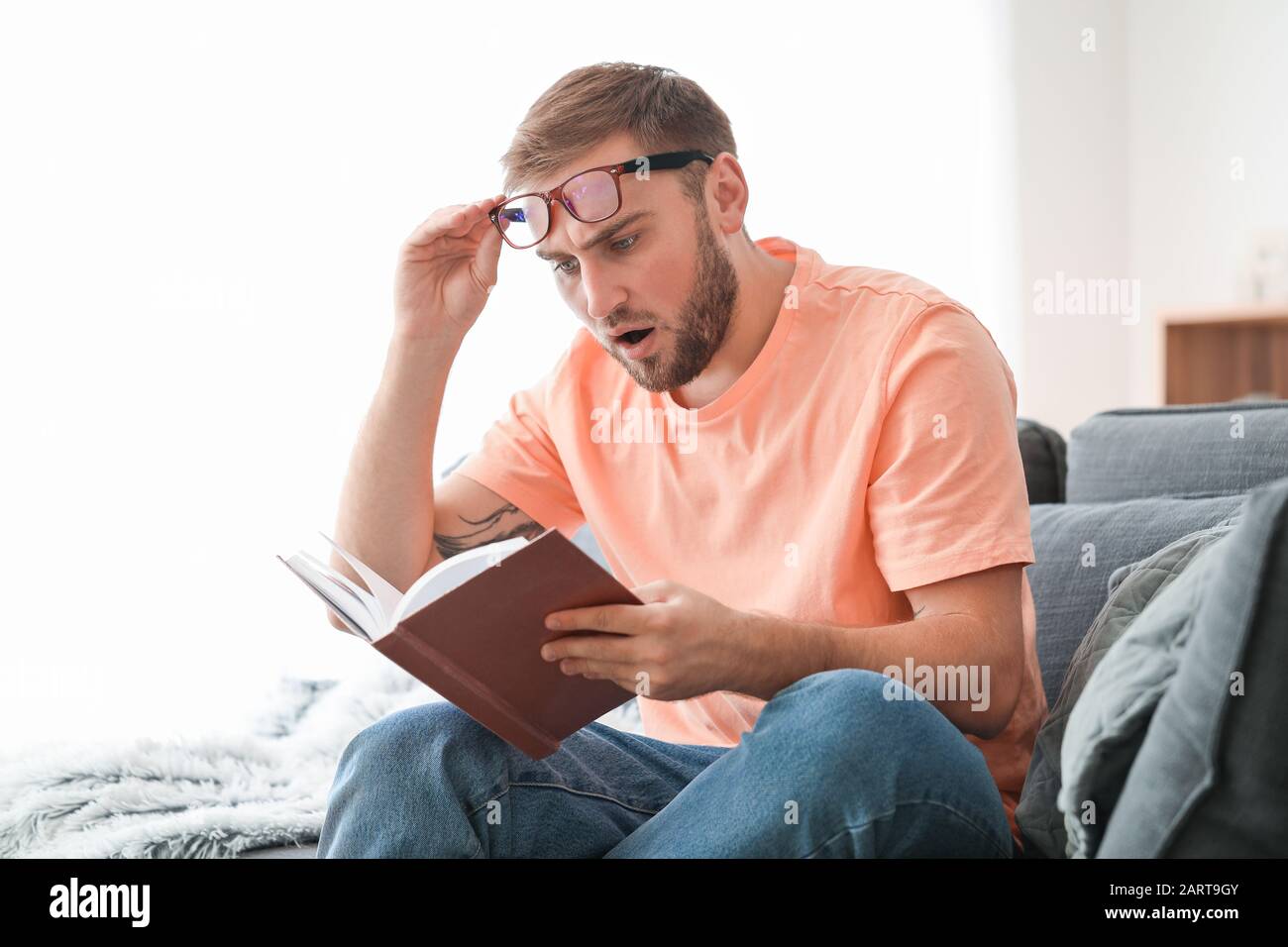 Worried young man reading book at home Stock Photo - Alamy