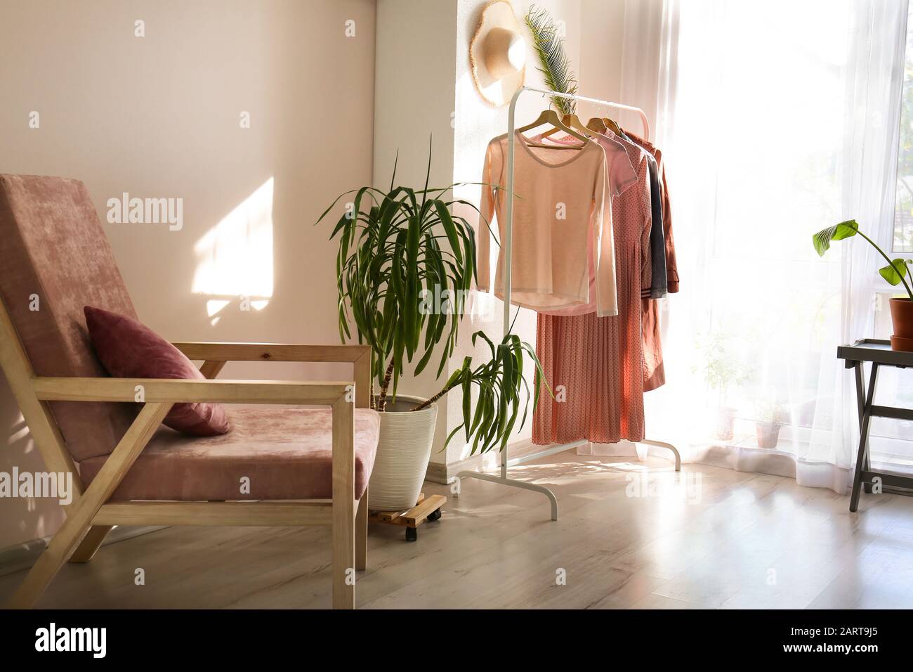 Rack with hanging clothes near window in room Stock Photo - Alamy