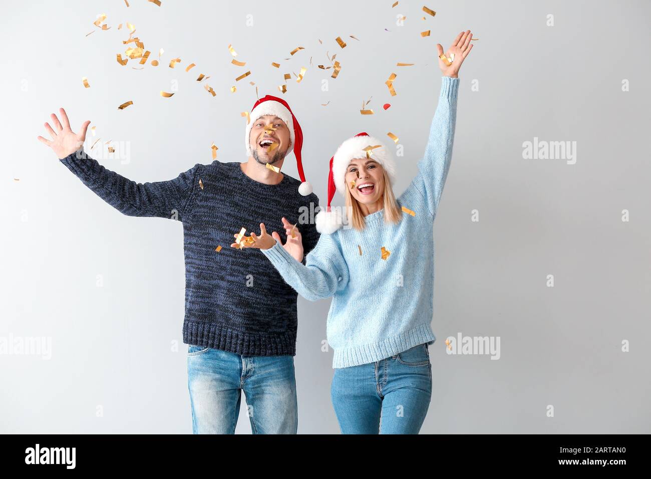 Happy couple in Santa hats and falling confetti on light background ...
