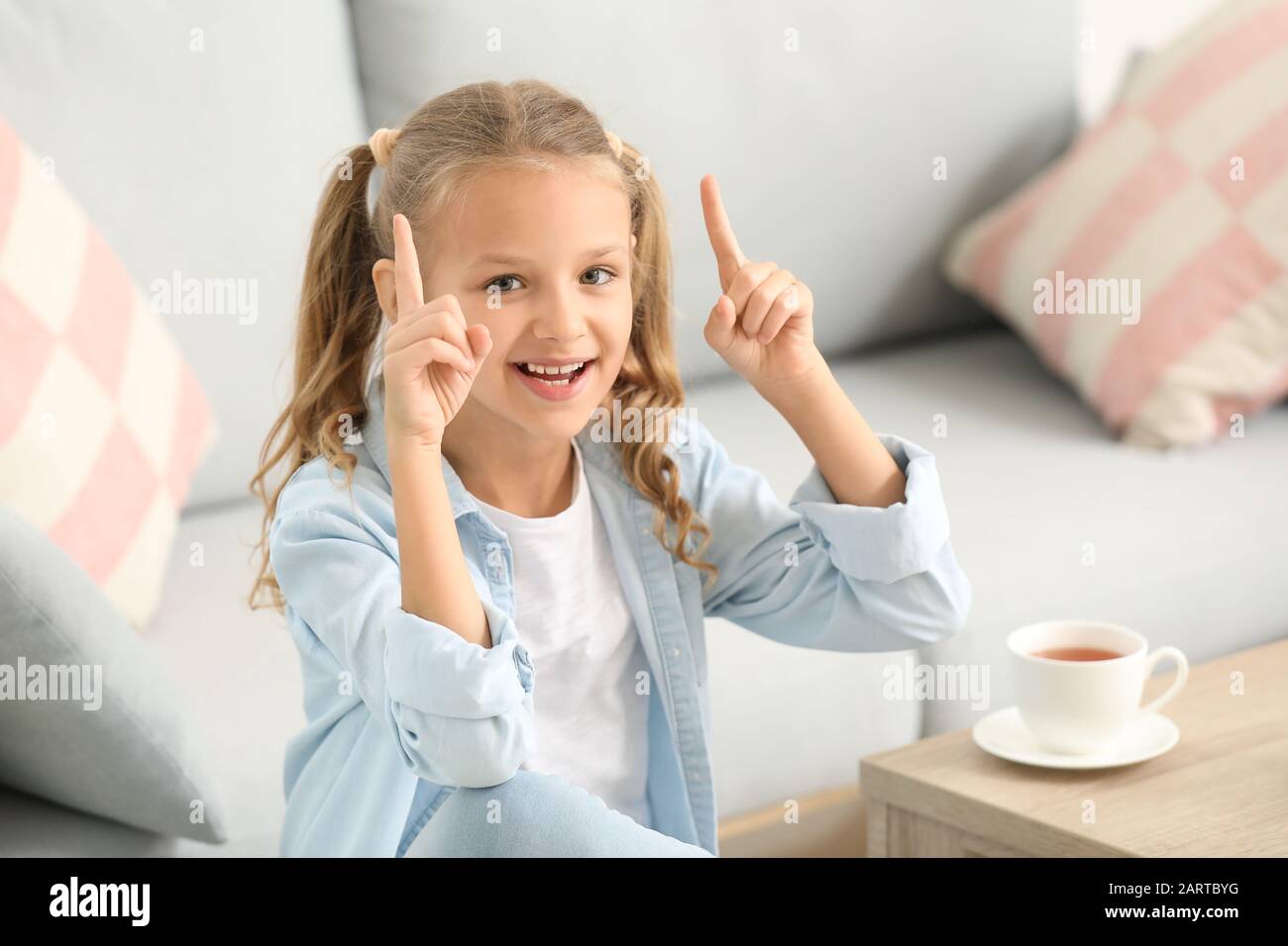 Cute little girl with raised index fingers at home Stock Photo - Alamy