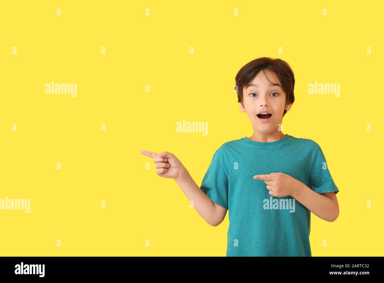 Surprised little boy pointing at something on color background Stock ...