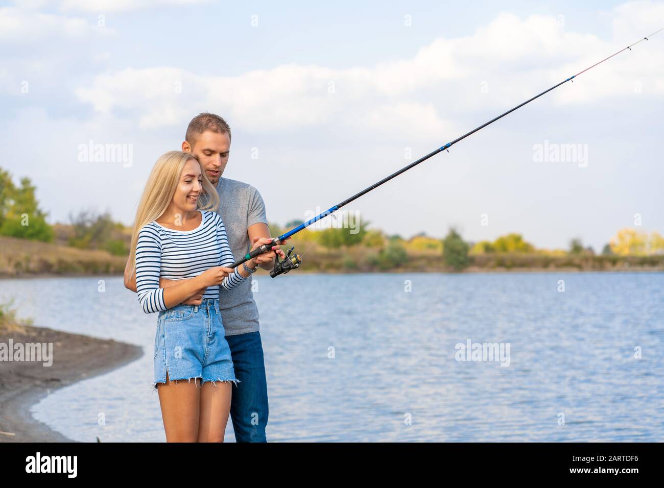 Happy young couple fishing by lakeside Stock Photo - Alamy