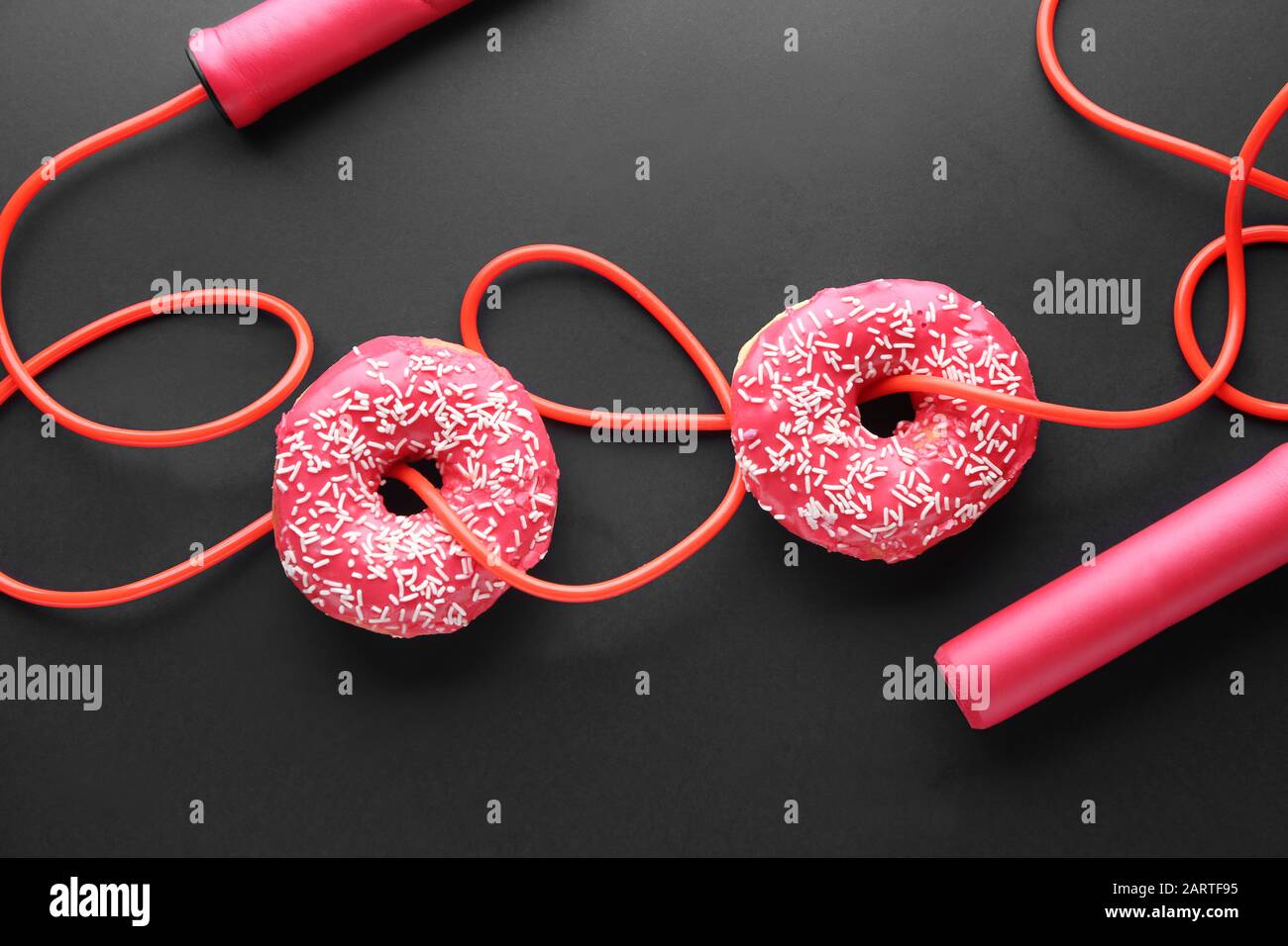 Creative composition tasty donuts and jumping rope on dark background ...