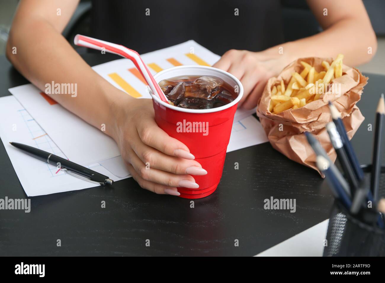 Woman drinking cold cola and eating french fries at table in office ...