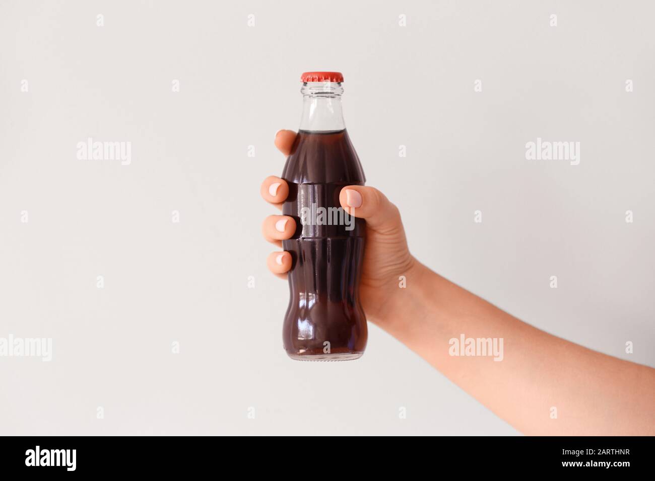 Female hand with bottle of cola on light background Stock Photo - Alamy