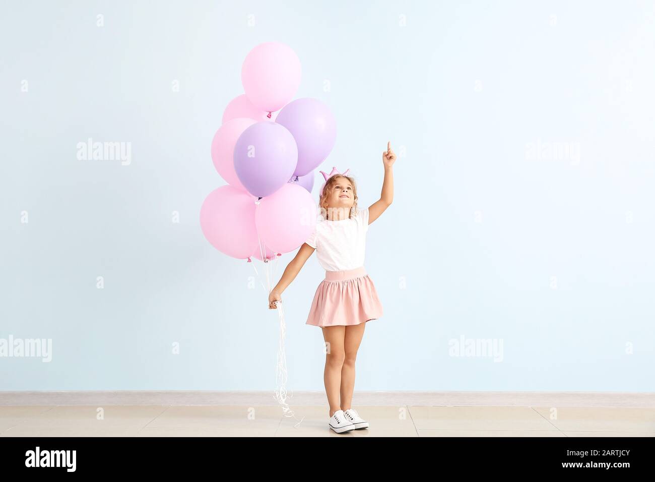 Little girl with balloons pointing at something near color wall Stock ...