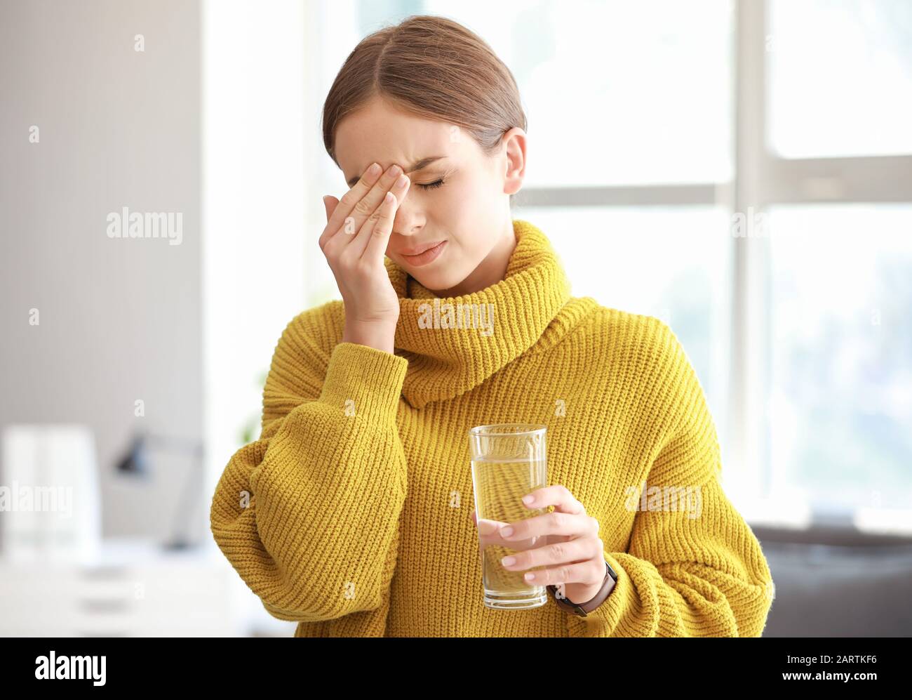 Young woman with glass of water suffering from headache at home Stock ...