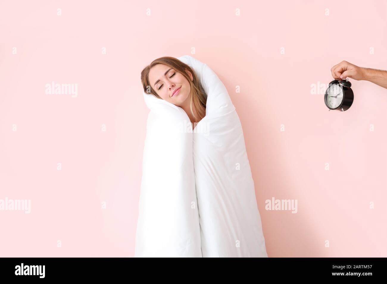 Sleepy young woman wrapped in blanket and male hand with alarm clock on ...