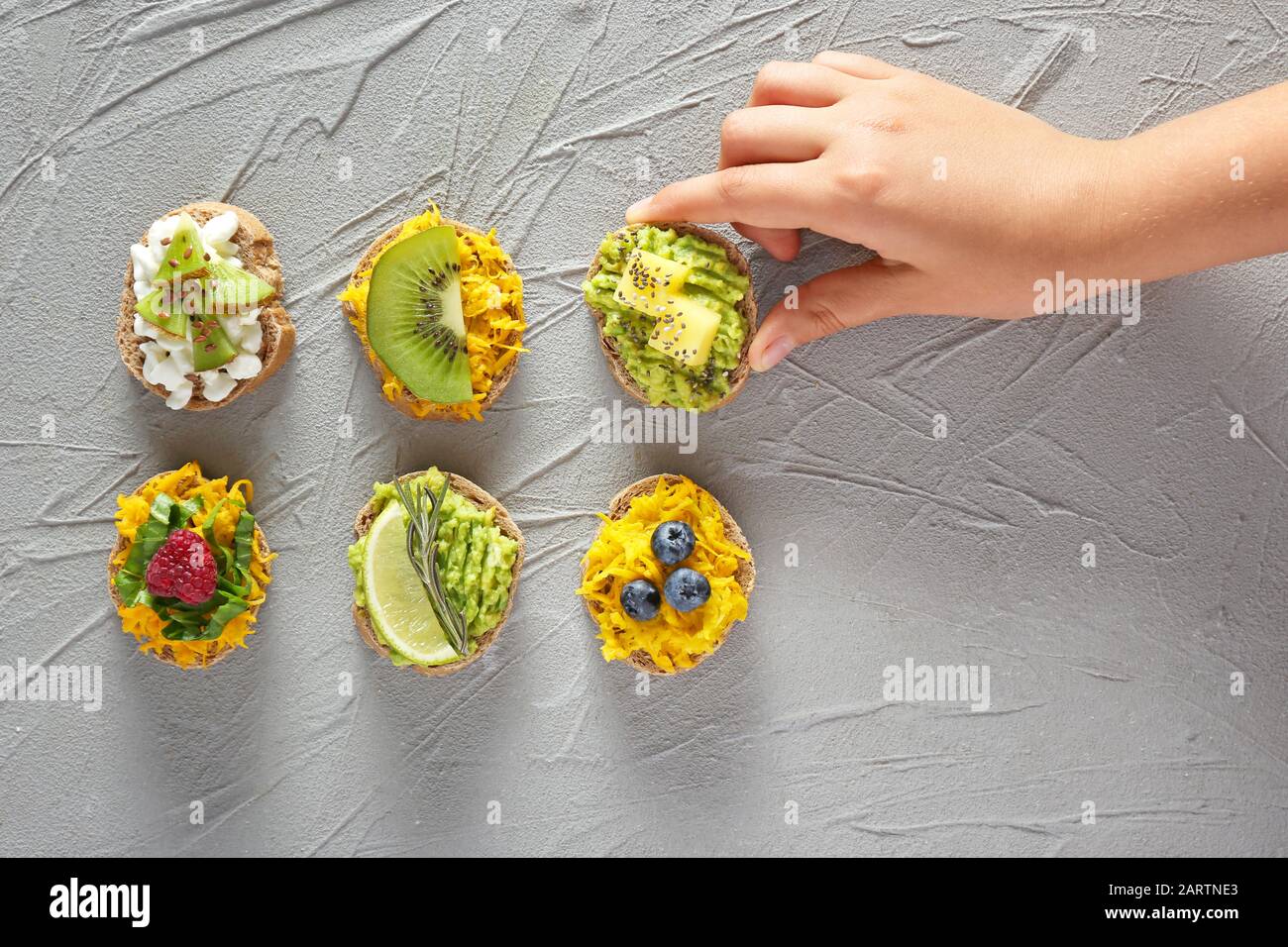 Female hand with tasty sandwiches on grey background Stock Photo - Alamy