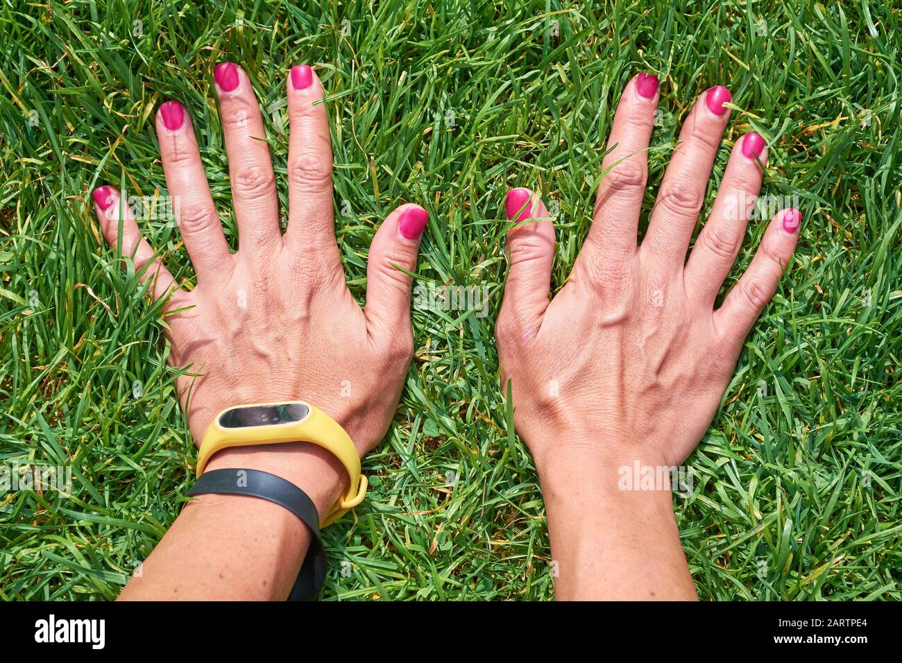 Woman hands spread out in green grass, with a yellow tech band around ...
