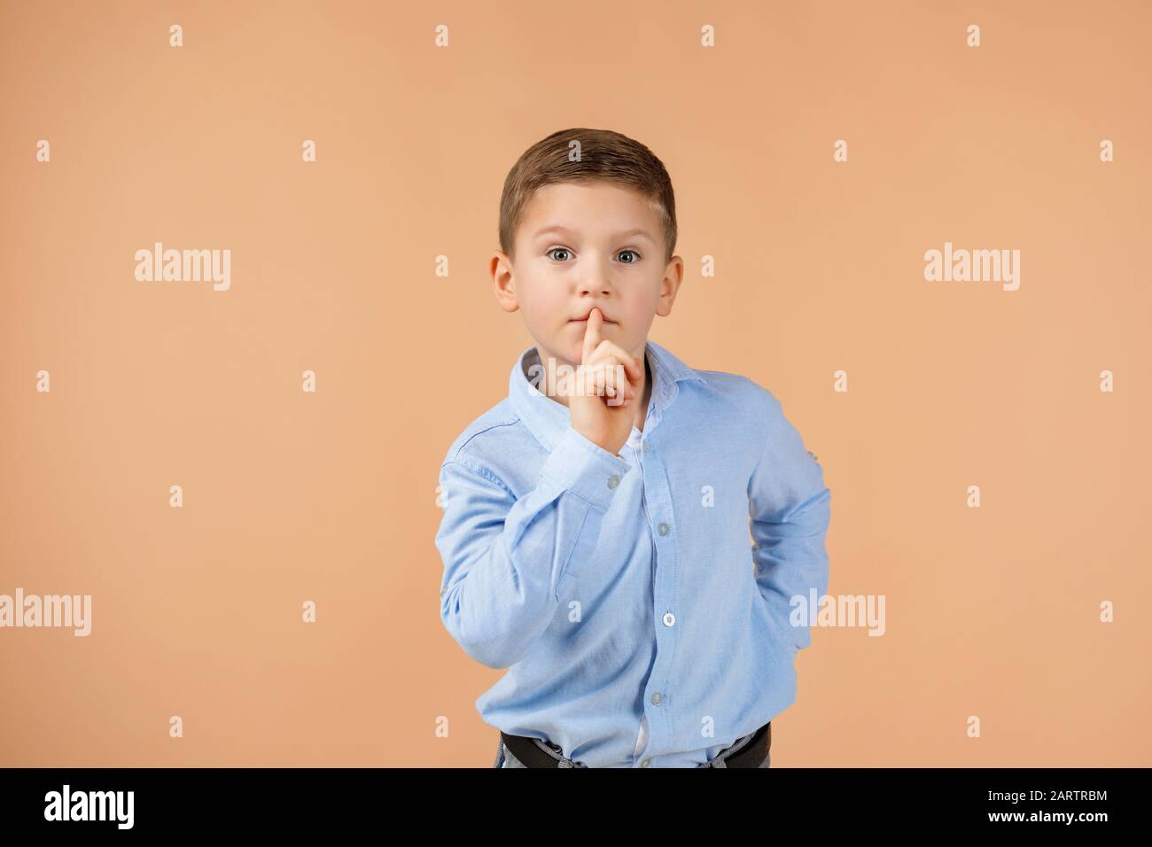 cute little boy in blue shirt asking to be quiet with finger on lips on ...