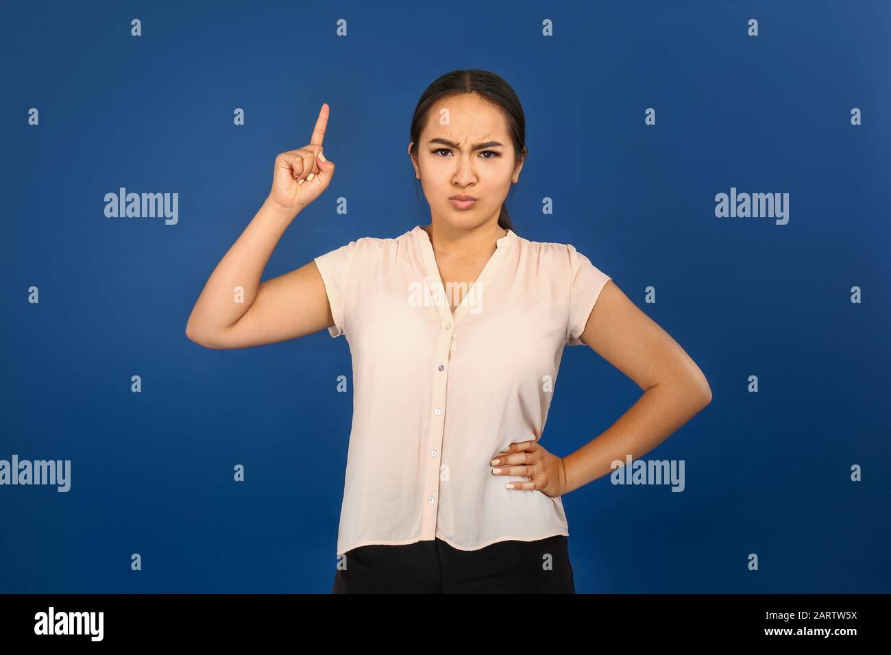 Portrait of angry Asian woman with raised index finger on color ...