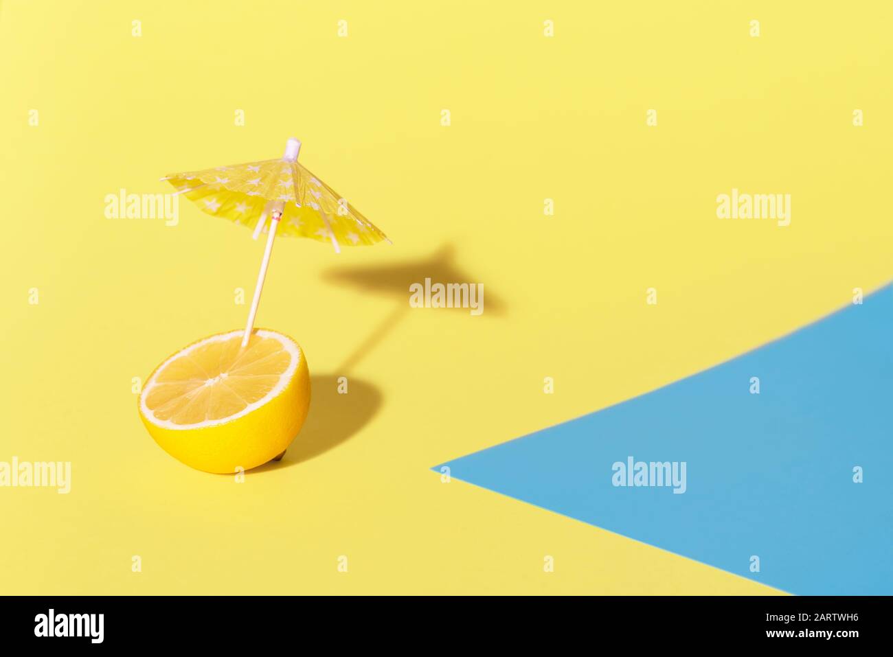 Lemon with a cocktail umbrella in it, in sunlight, on a yellow ...
