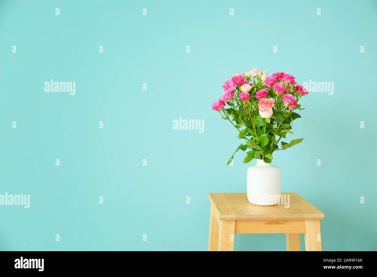 Vase with beautiful rose flowers on stool against color background ...