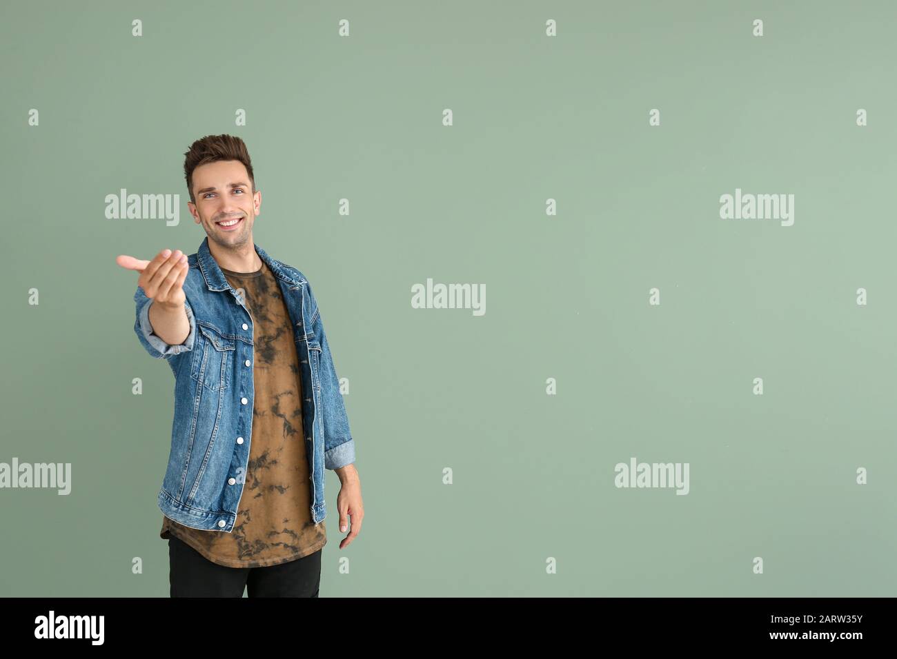 Handsome young man inviting viewer on color background Stock Photo - Alamy
