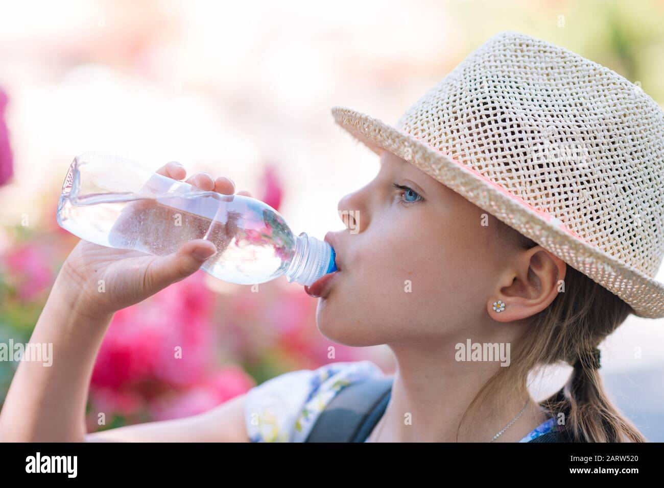 Little girl in a straw hat drinking water in a flower garden Stock ...