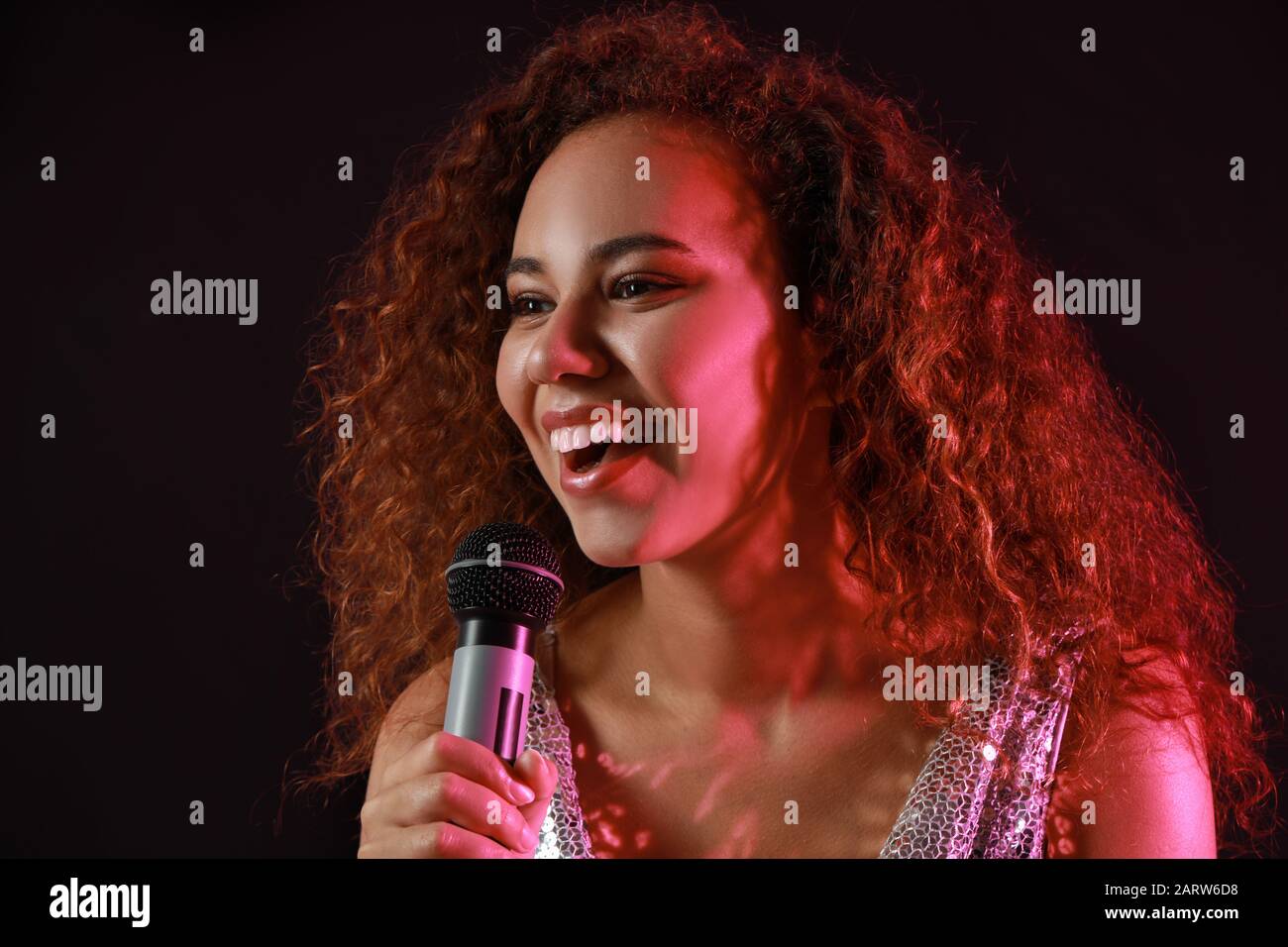 Beautiful African-American female singer with microphone on dark ...