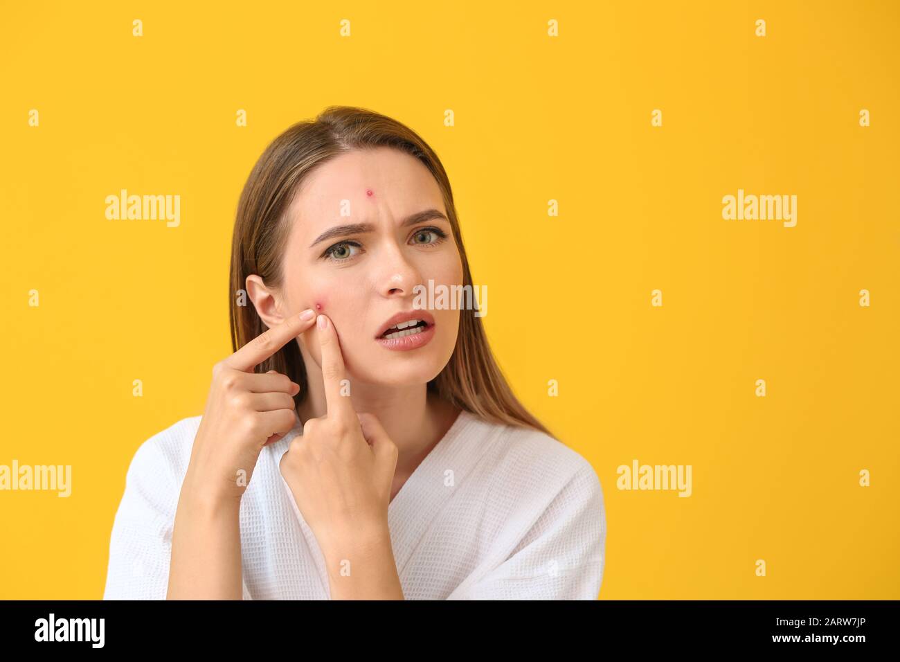 Portrait of young woman with acne problem squishing pimples on color ...