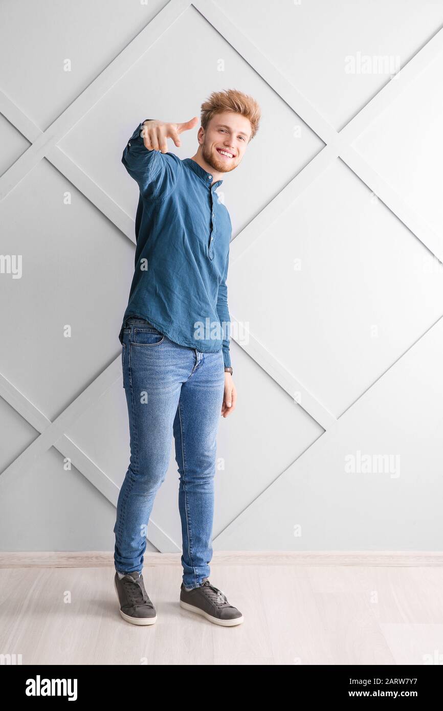 Portrait of young man pointing at viewer near grey wall Stock Photo - Alamy