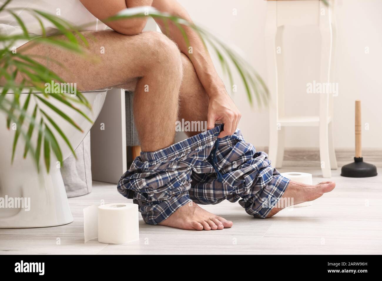 Young man sitting on toilet bowl at home Stock Photo - Alamy