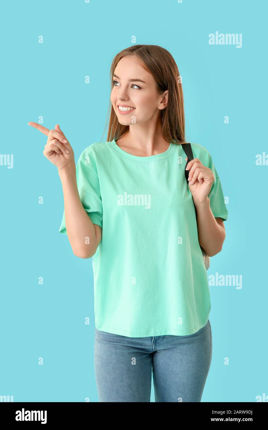 Beautiful female student pointing at something on color background ...