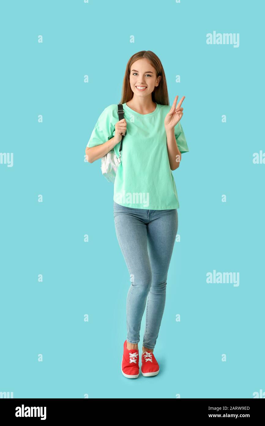 Beautiful female student showing victory gesture on color background ...